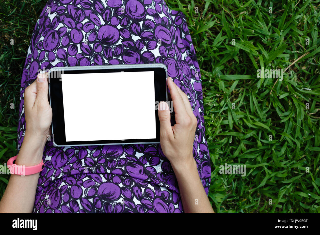 Anonymous woman in purple dress relaxing on green grass with tablet ...