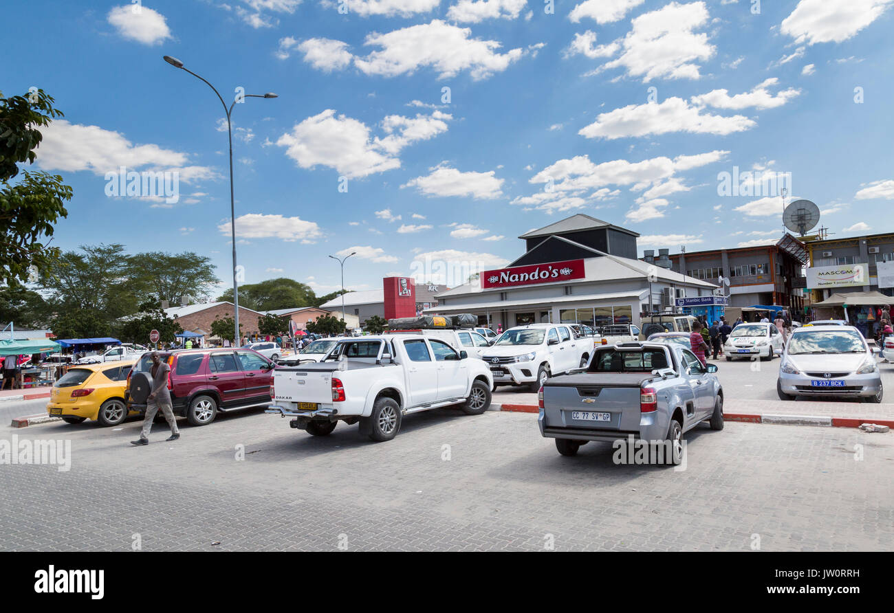 A small shopping center in central Maun with vehicles parked in a paved ...