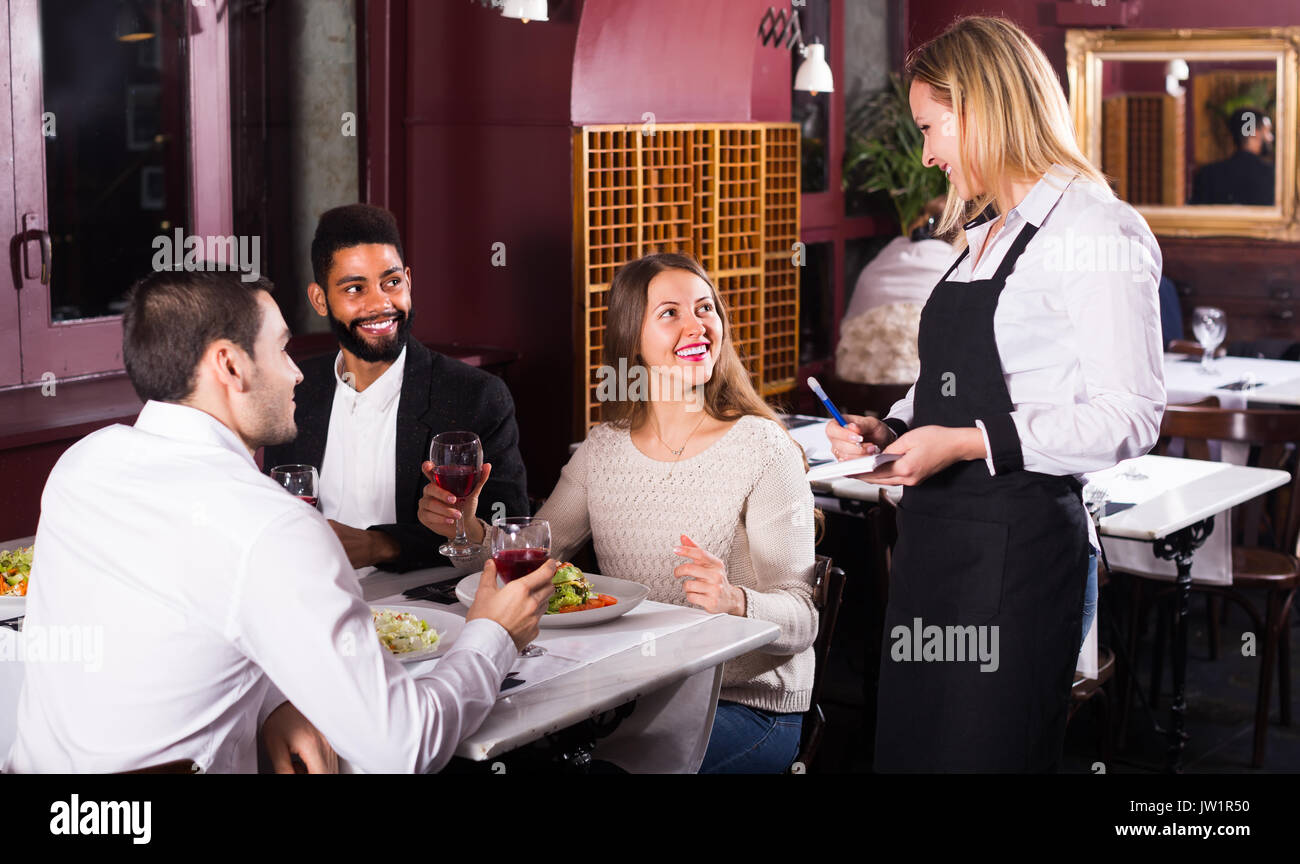 Positive smiling young waitress taking order from restaurant guests at ...