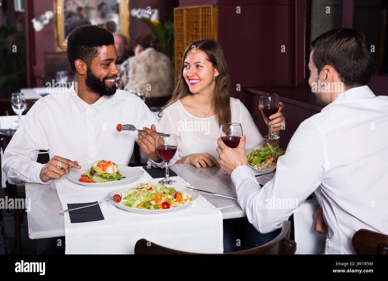 Three friends eating at restaurant table and chatting Stock Photo - Alamy