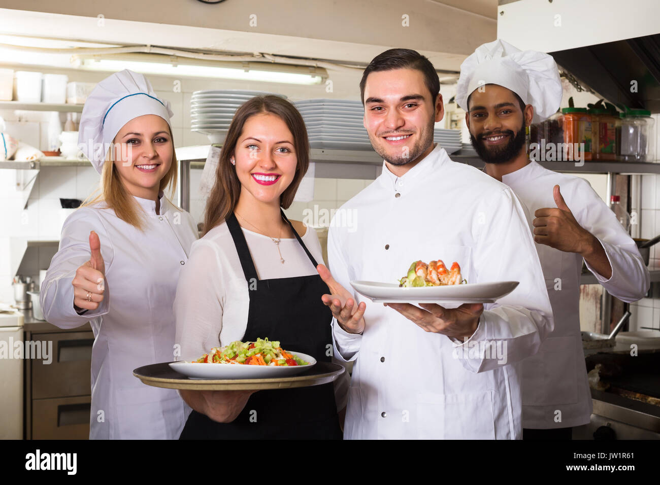 Positive smiling waitress and cooking team at professional kitchen in ...