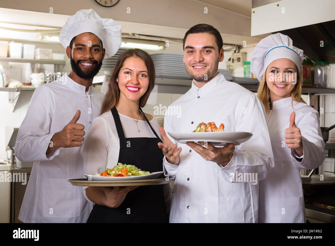 happy waitress and crew of professional cooks posing at restaurant ...