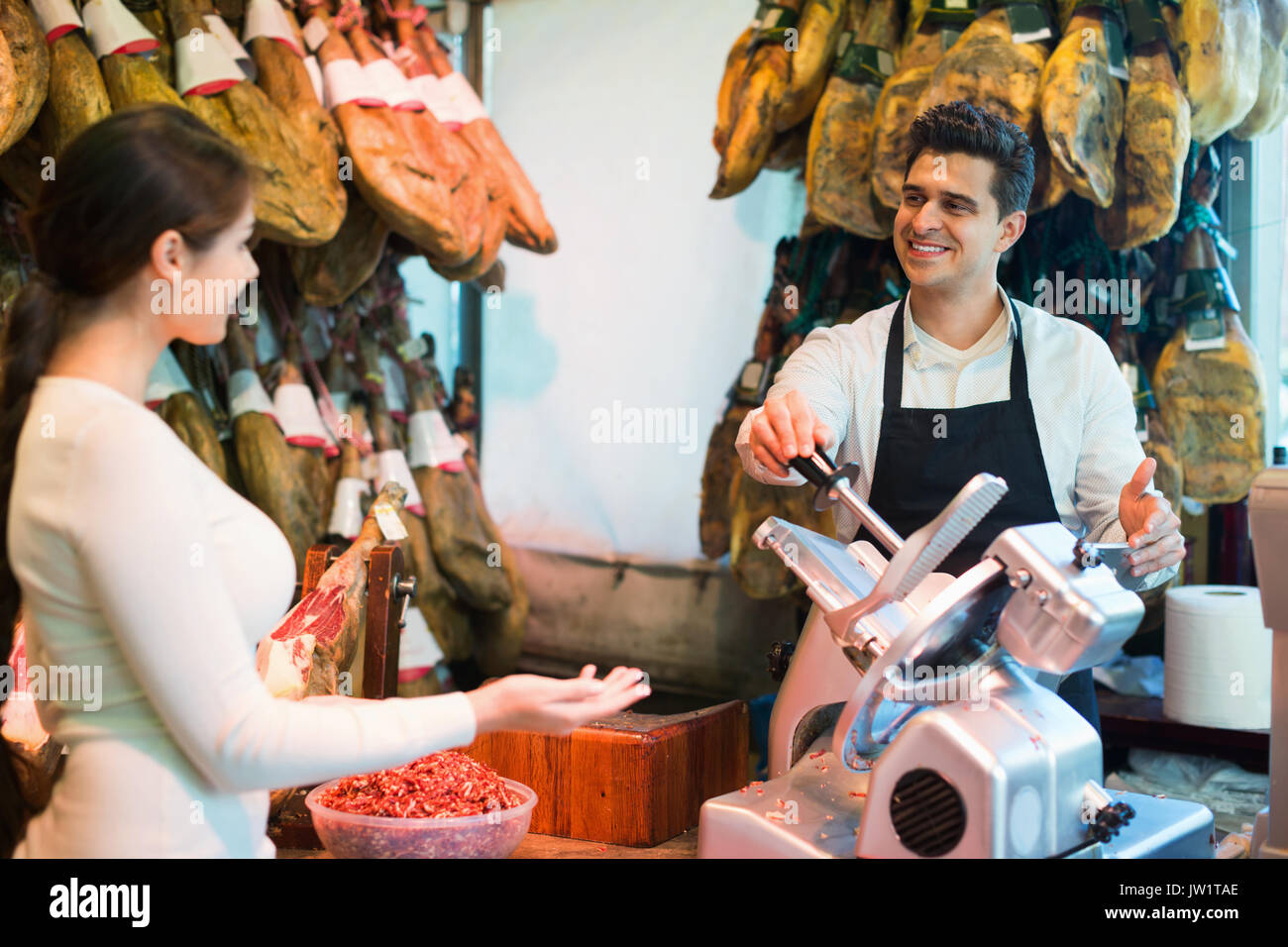 Young cute brunette choosing iberico and serrano jamon and smiling ...