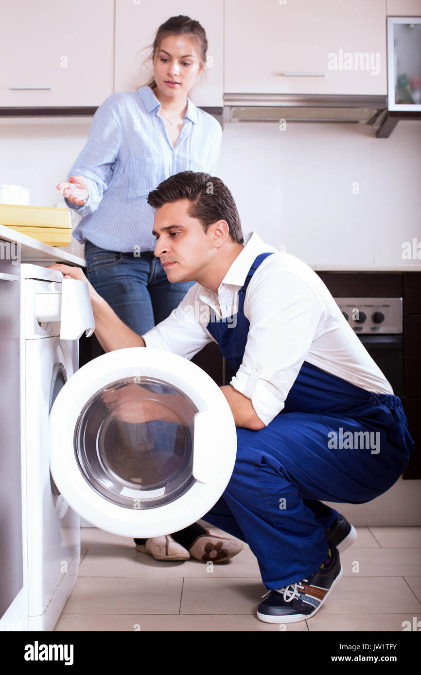 Professional mechanic repairing washing machine at clients kitchen ...