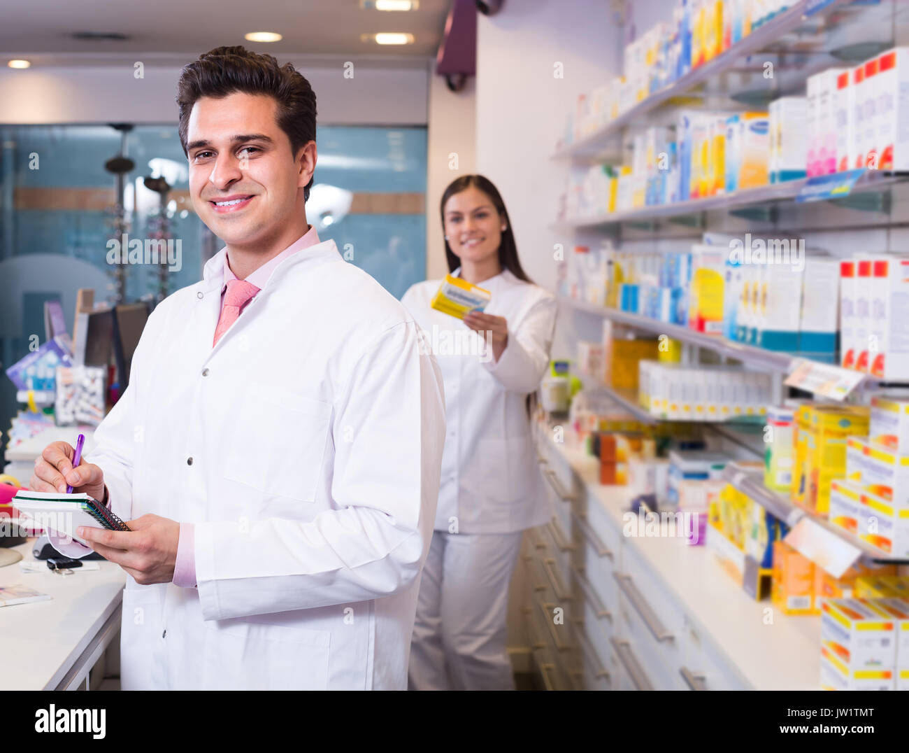 Two positive smiling pharmacists in uniform at the work in modern ...