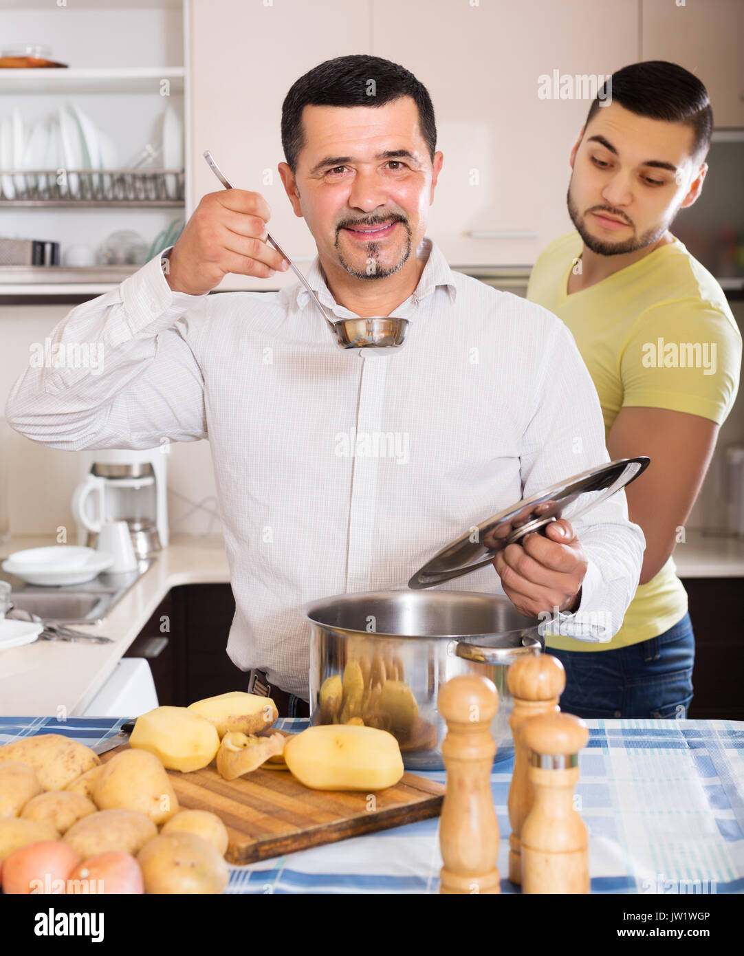 Son helping positive father to prepare vegetable stew at kitchen Stock ...