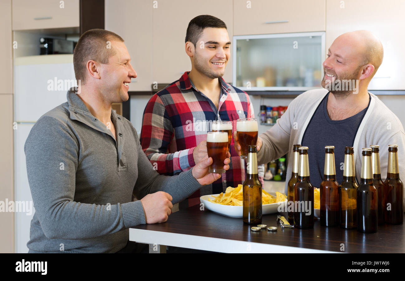 Three fun guys drinking beer,eating chips and laughing at house party ...