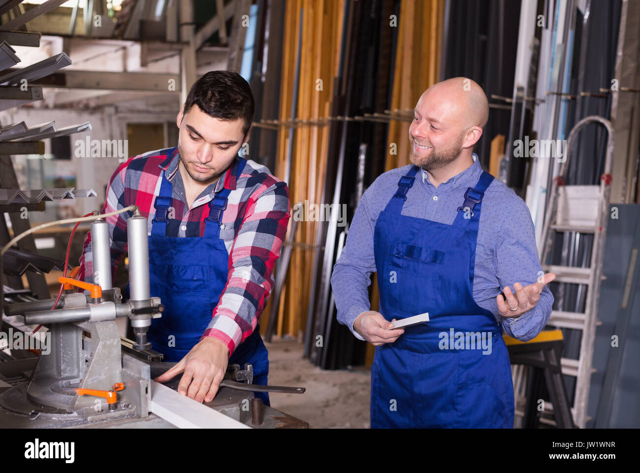 Two workmen in uniform working on machine in PVC shop indoor Stock ...