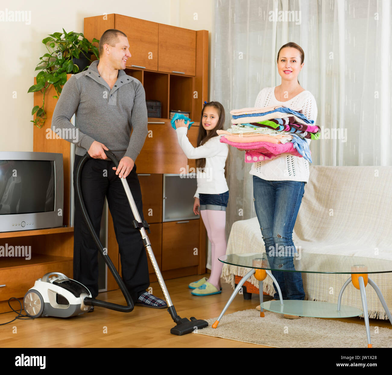Cheerful family of three cleaning up at home all together. Focus on man ...