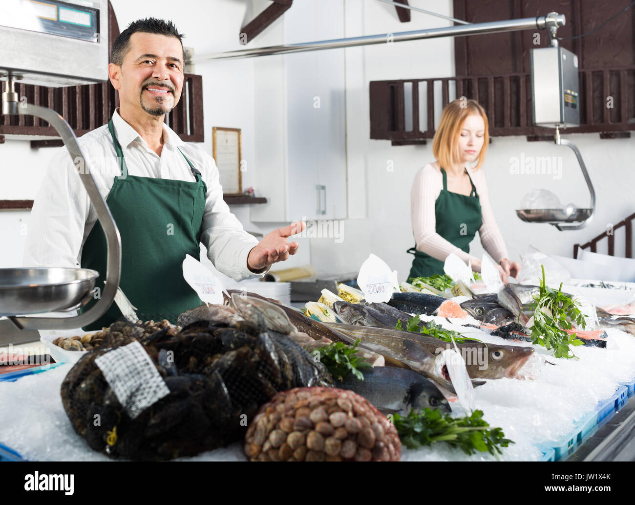 Portrait of two positive sellers in aprons working in fish section of ...