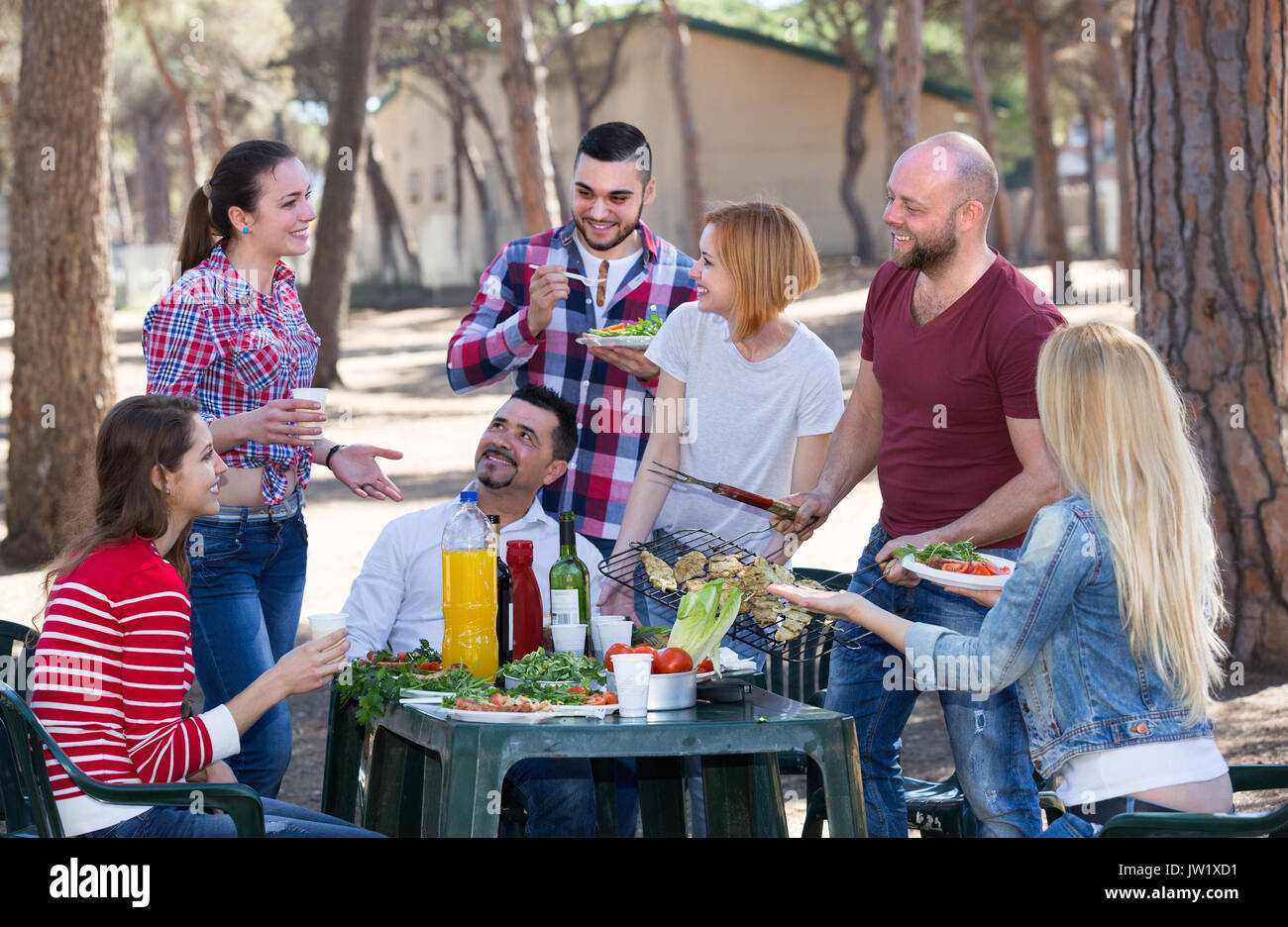 Positive colleagues making grill at summer corporate party outdoors ...