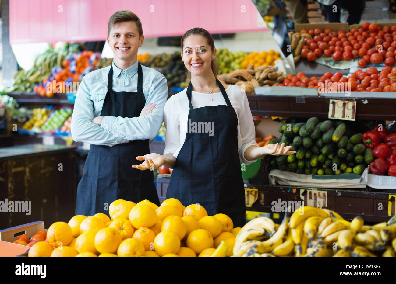 Happy smiling positive sellers having vegetables and fruits on displays ...