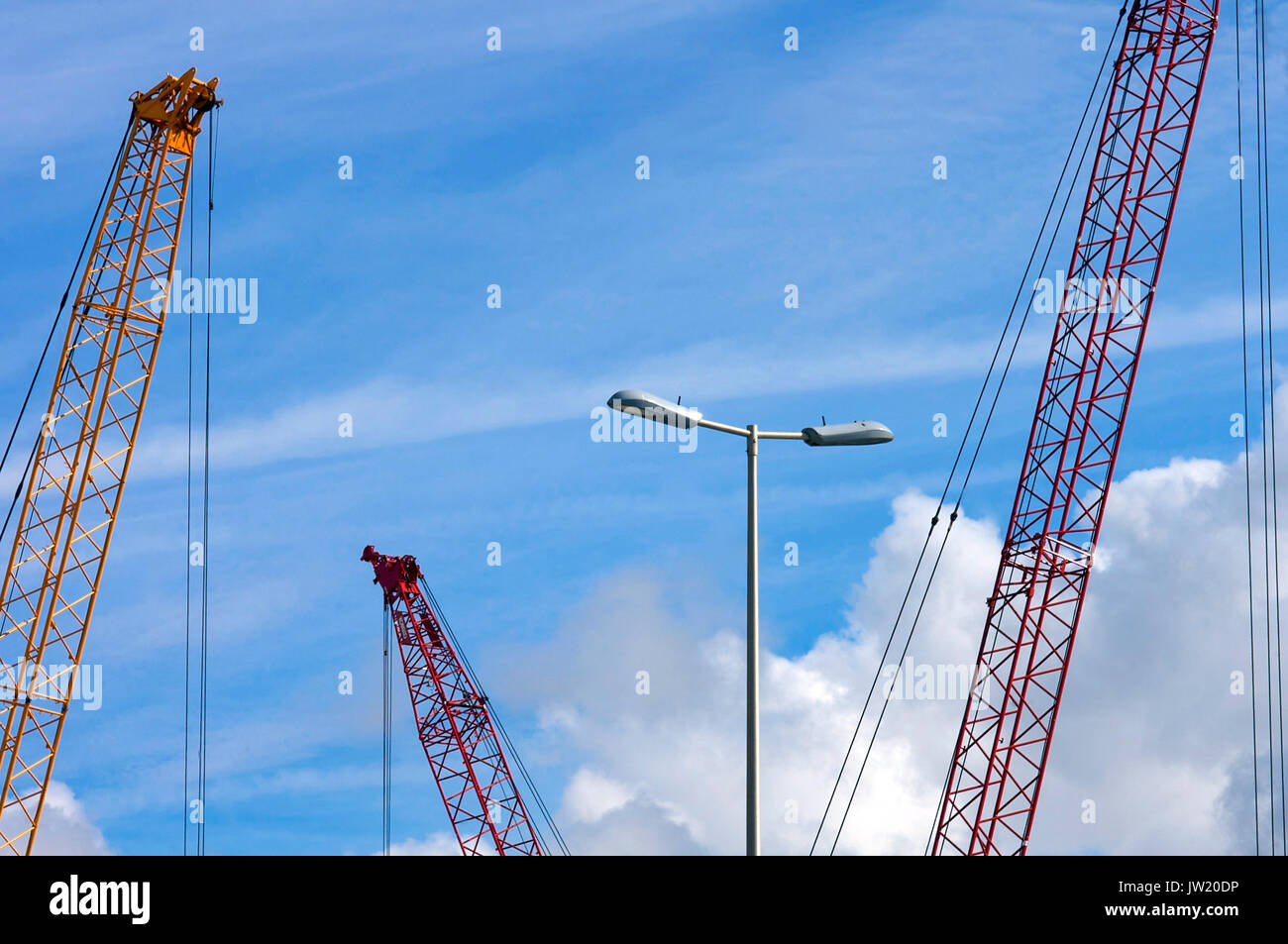 Three mechanical cranes and lamp post against blue sky Stock Photo - Alamy