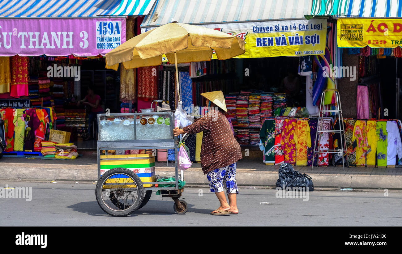 A female Vietnamese street vendor pushes a cart along a street in Ho ...