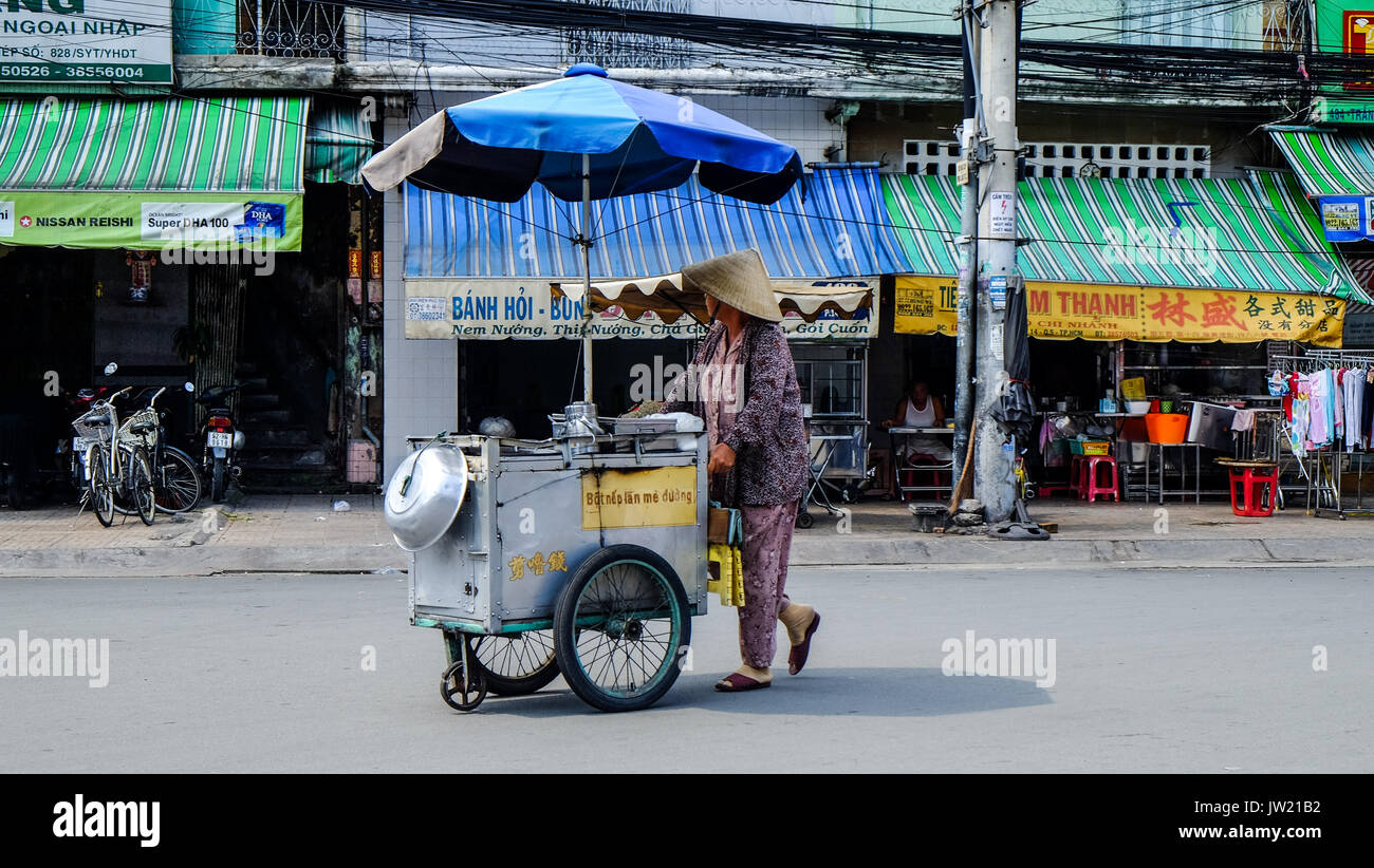 A female Vietnamese street vendor pushes a cart along a street in Ho ...