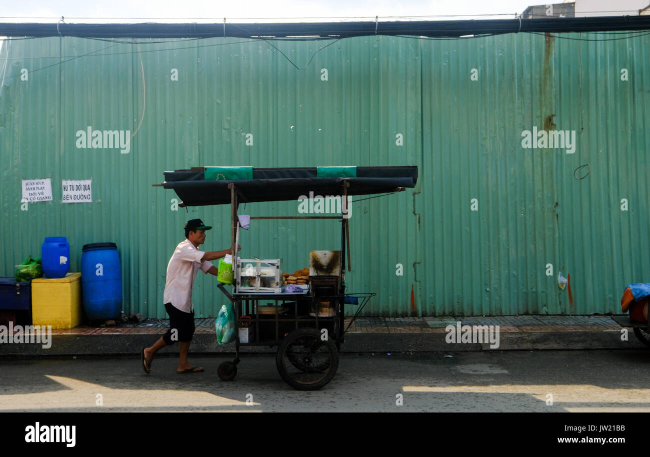A male Vietnamese street vendor pushes his cart along a street in Ho ...
