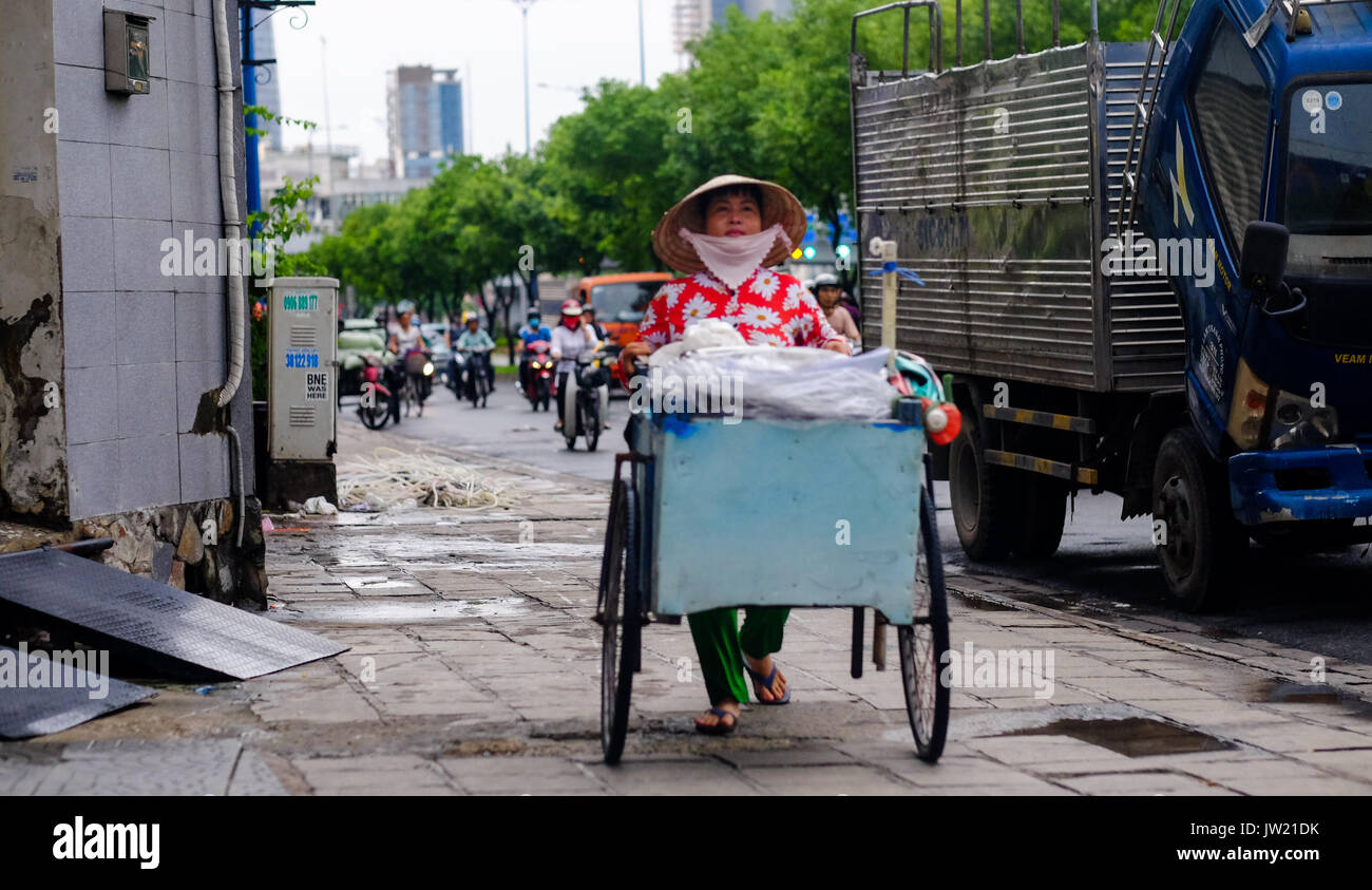 A female Vietnamese street vendor pushes a cart along a street in Ho ...