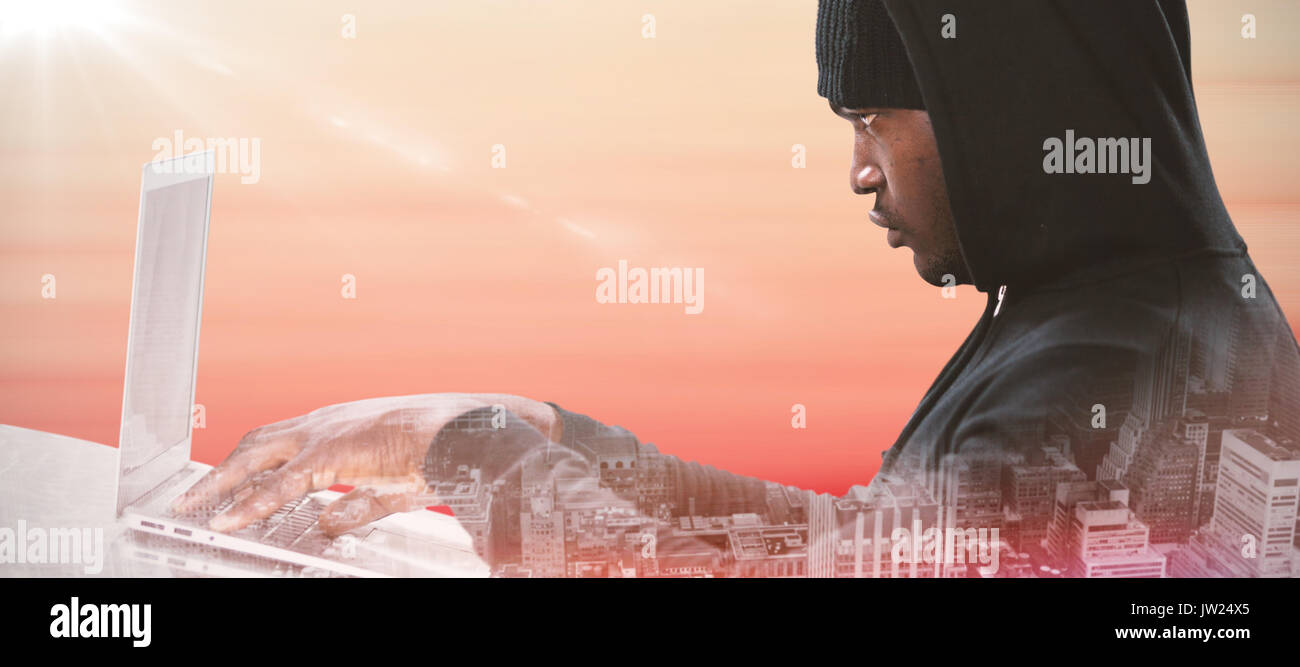 Male hacker using laptop against orange and yellow abstract backgrounds ...