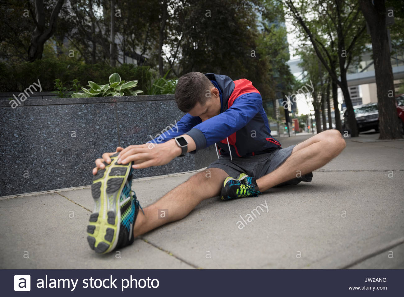 Male runner stretching leg on urban sidewalk Stock Photo - Alamy