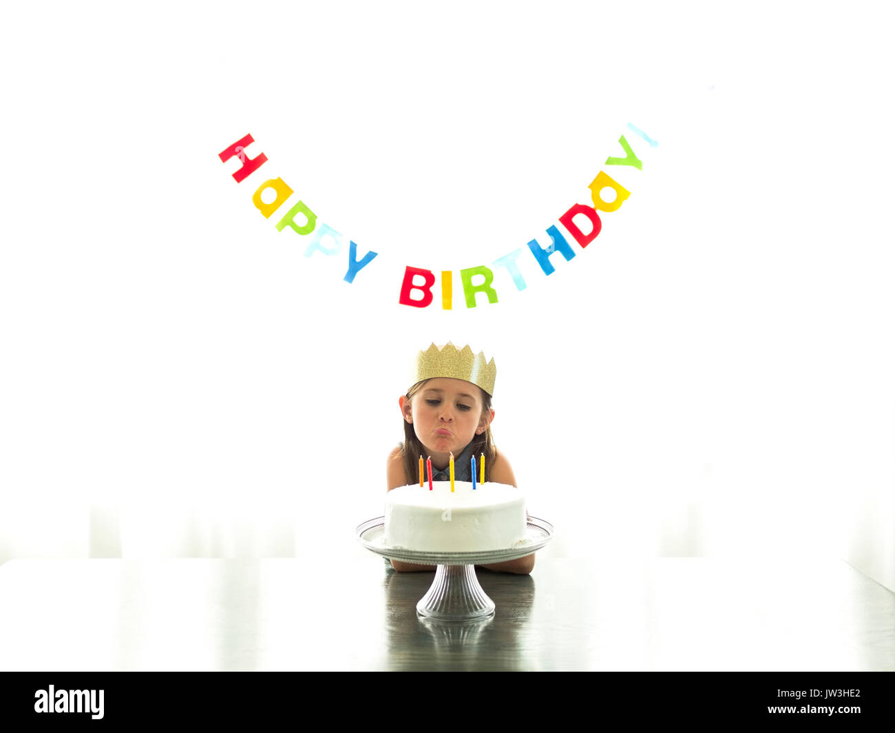 Girl (6-7) in paper crown blowing candles on birthday cake Stock Photo ...