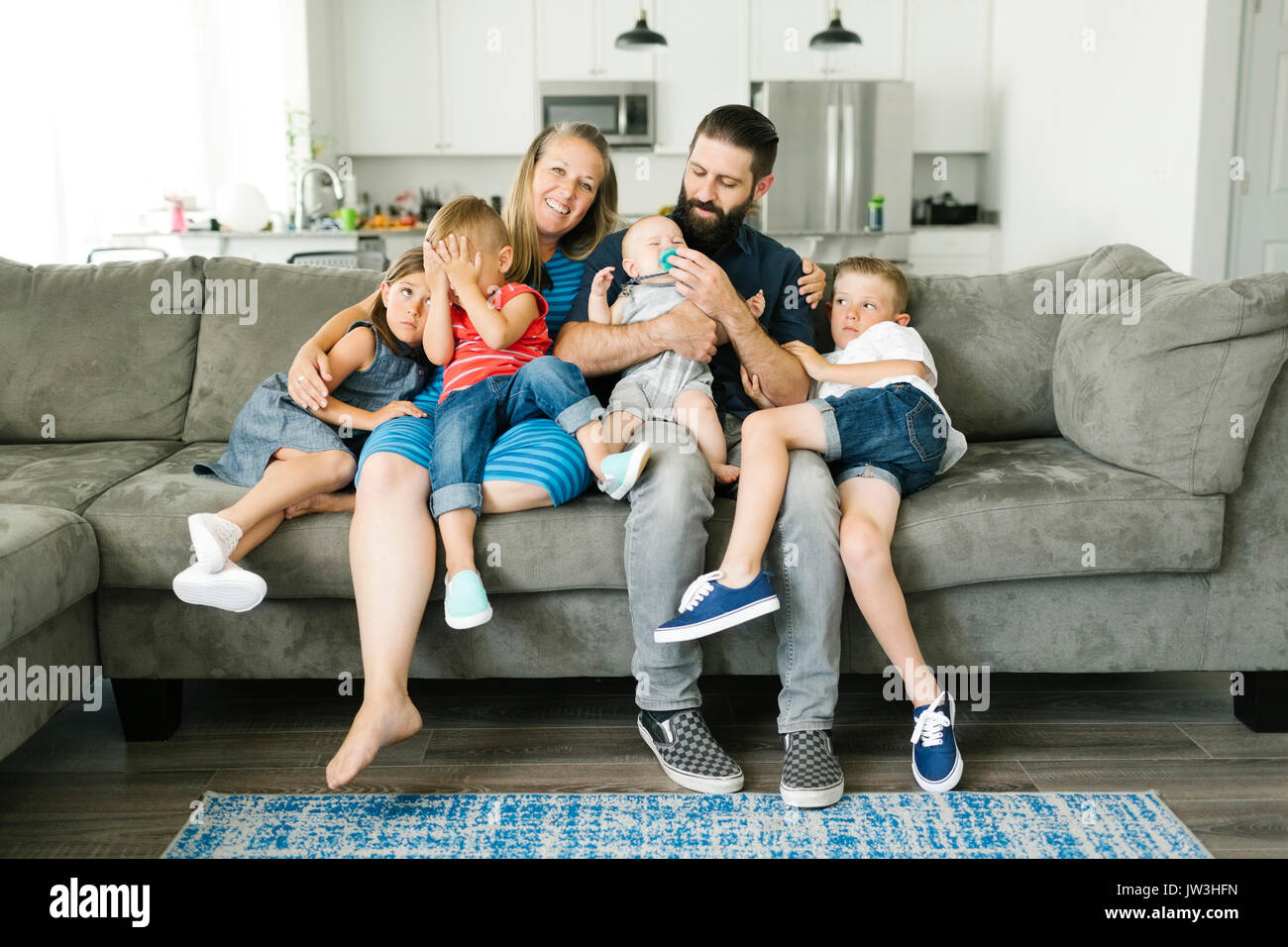 Family with four children (6-11 months, 2-3, 6-7) spending time on sofa ...