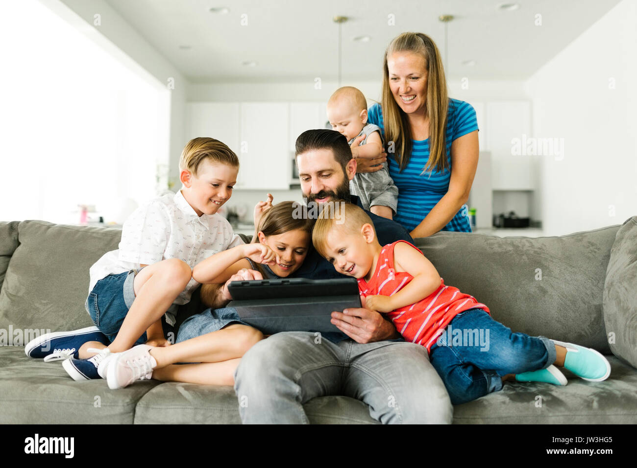 Family with four children (6-11 months, 2-3, 6-7) using digital tablet ...