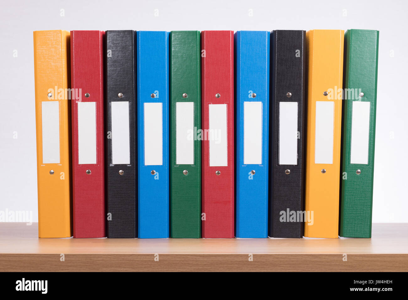 A row of multicoloured office document folders on a timber book shelf ...