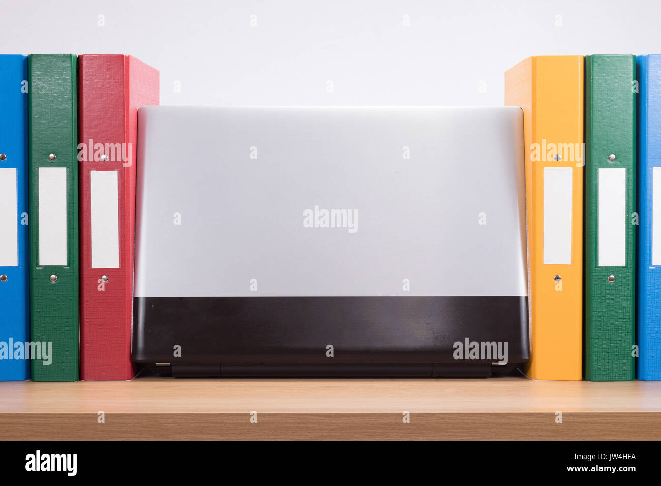 A computer laptop amongst a row of multicoloured office document ...