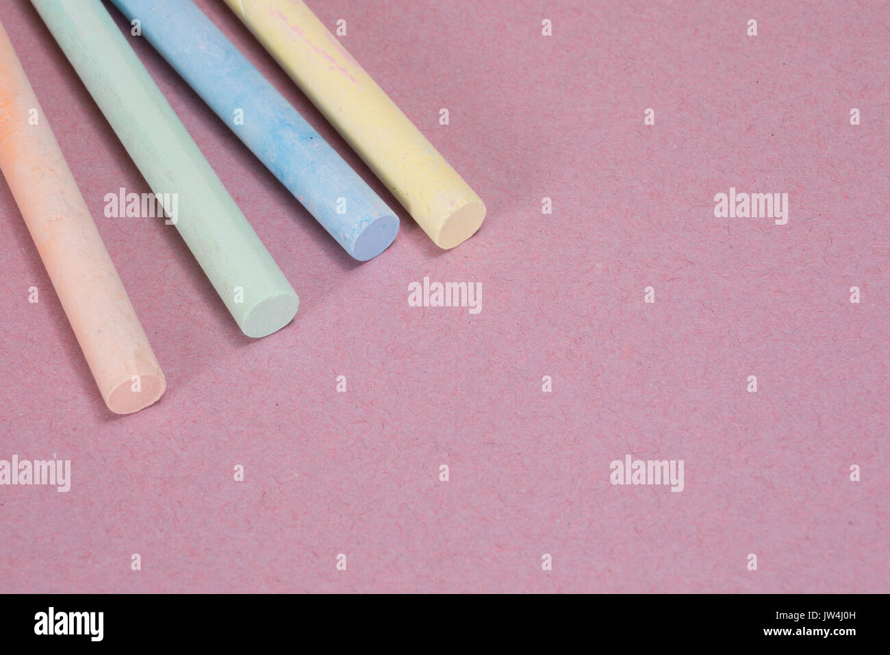 A close up of four chalk drawing sticks isolated on a plain pink ...
