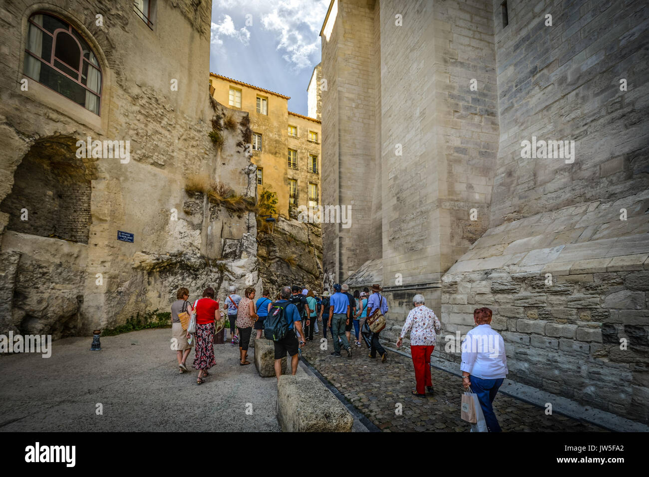 A group of tourists walk along a narrow stone path between a stone and ...