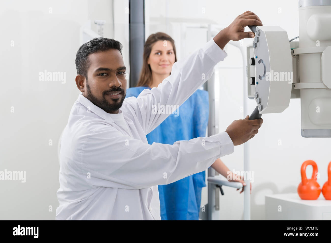 Portrait of male radiologist adjusting X-ray machine over female ...