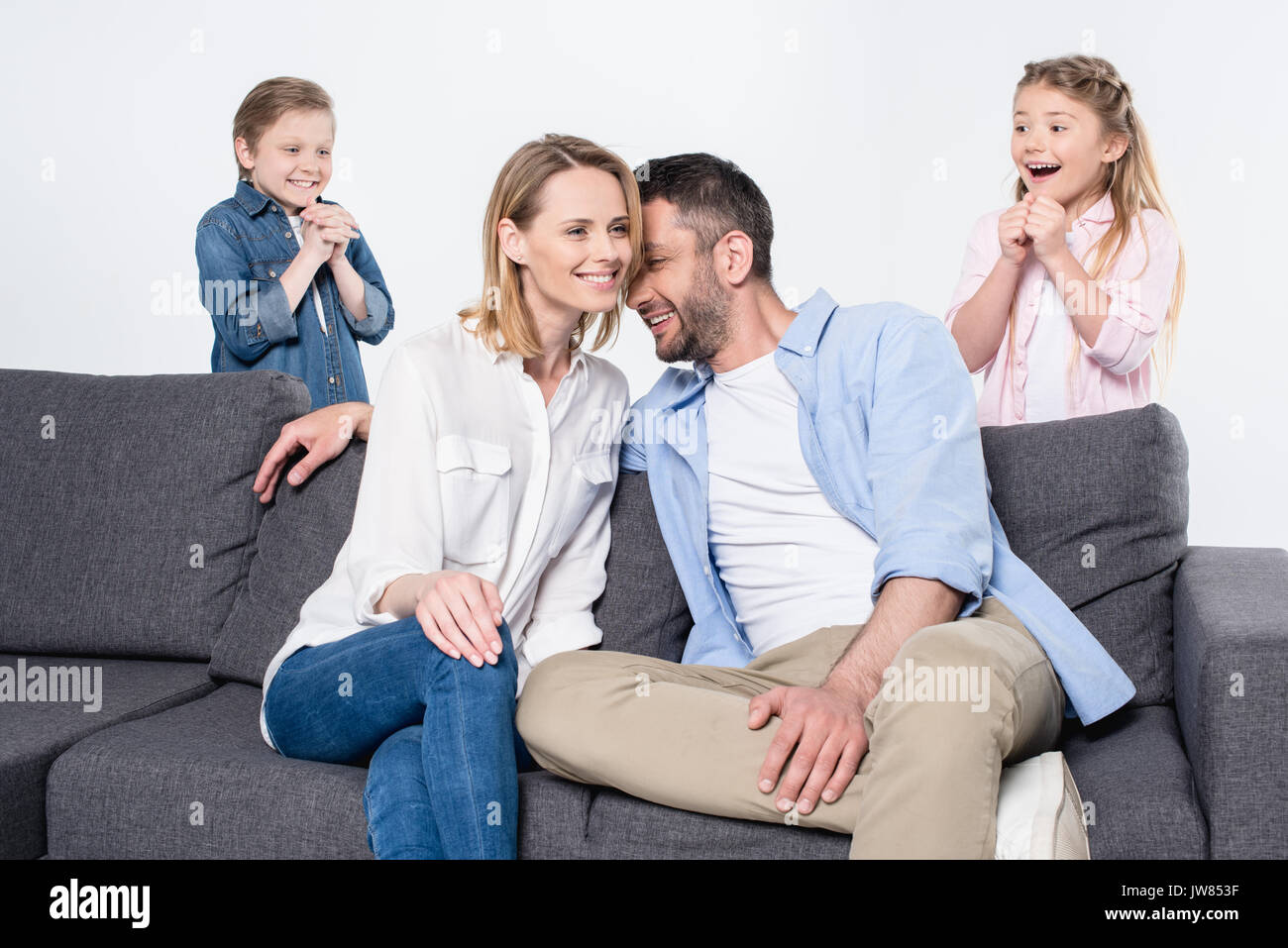 Cute cheerful children looking at happy parents sitting together on ...