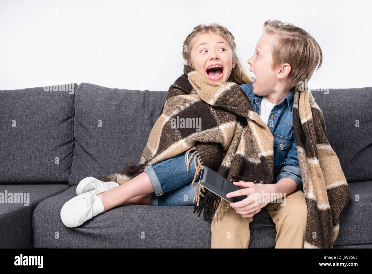 scared kids in blanket sitting on sofa and looking at each other ...