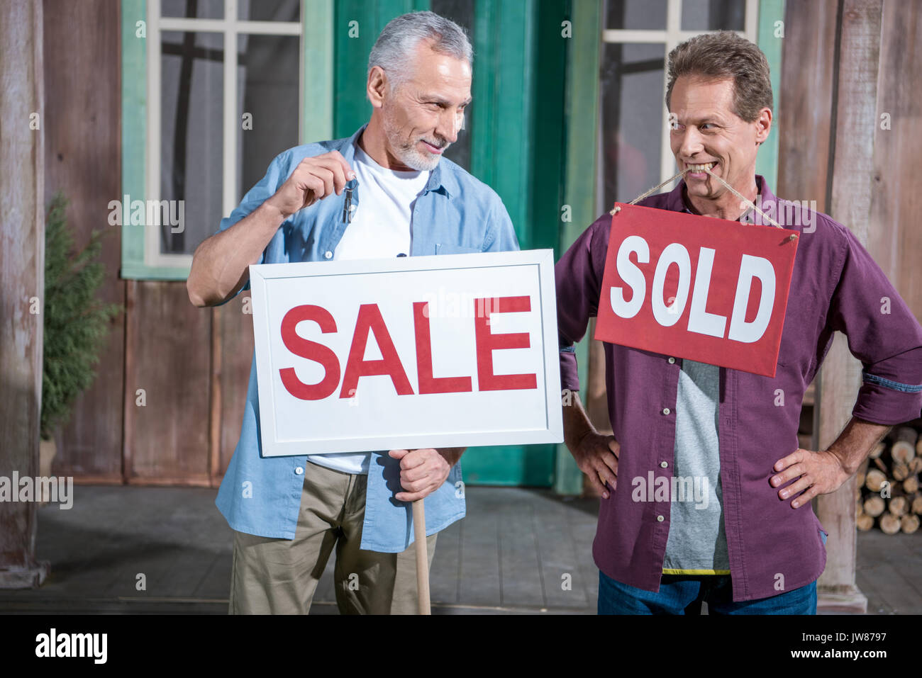 senior man holding sale sign while another man holding sold sing, house ...