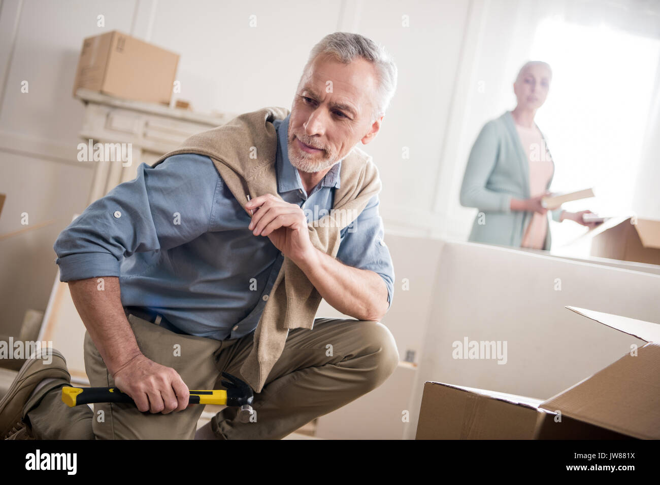 senior man sitting on floor with hammer in hand with wife behind Stock ...