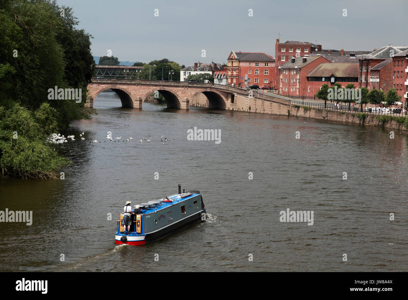 A canal narrowboat cruising on the river Severn in Worcester with Worcester Bridge in the ...