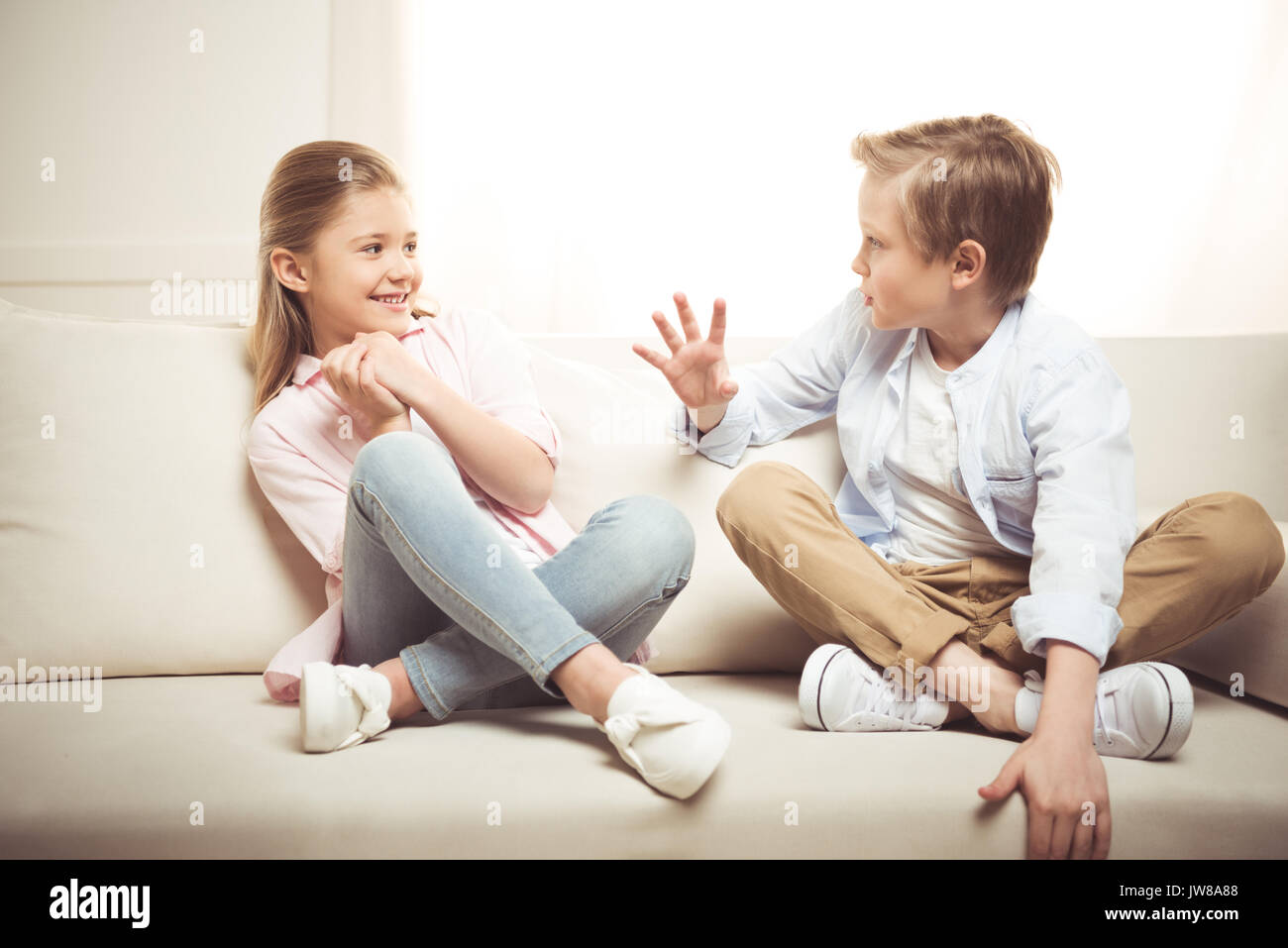 cheerful sister and brother talking together while sitting on sofa at ...