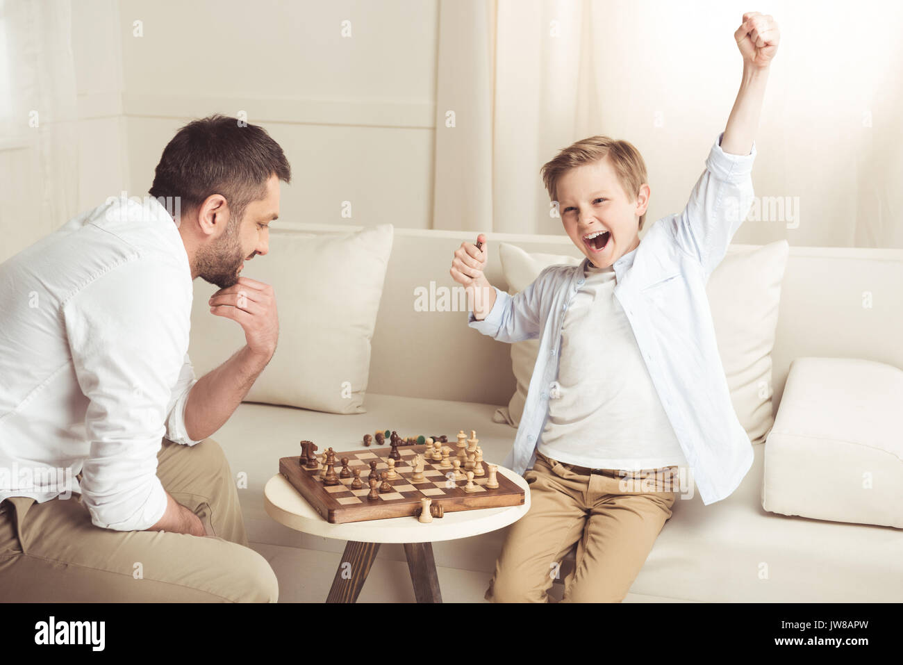 side view of boy celebrating success in chess game with father near by ...
