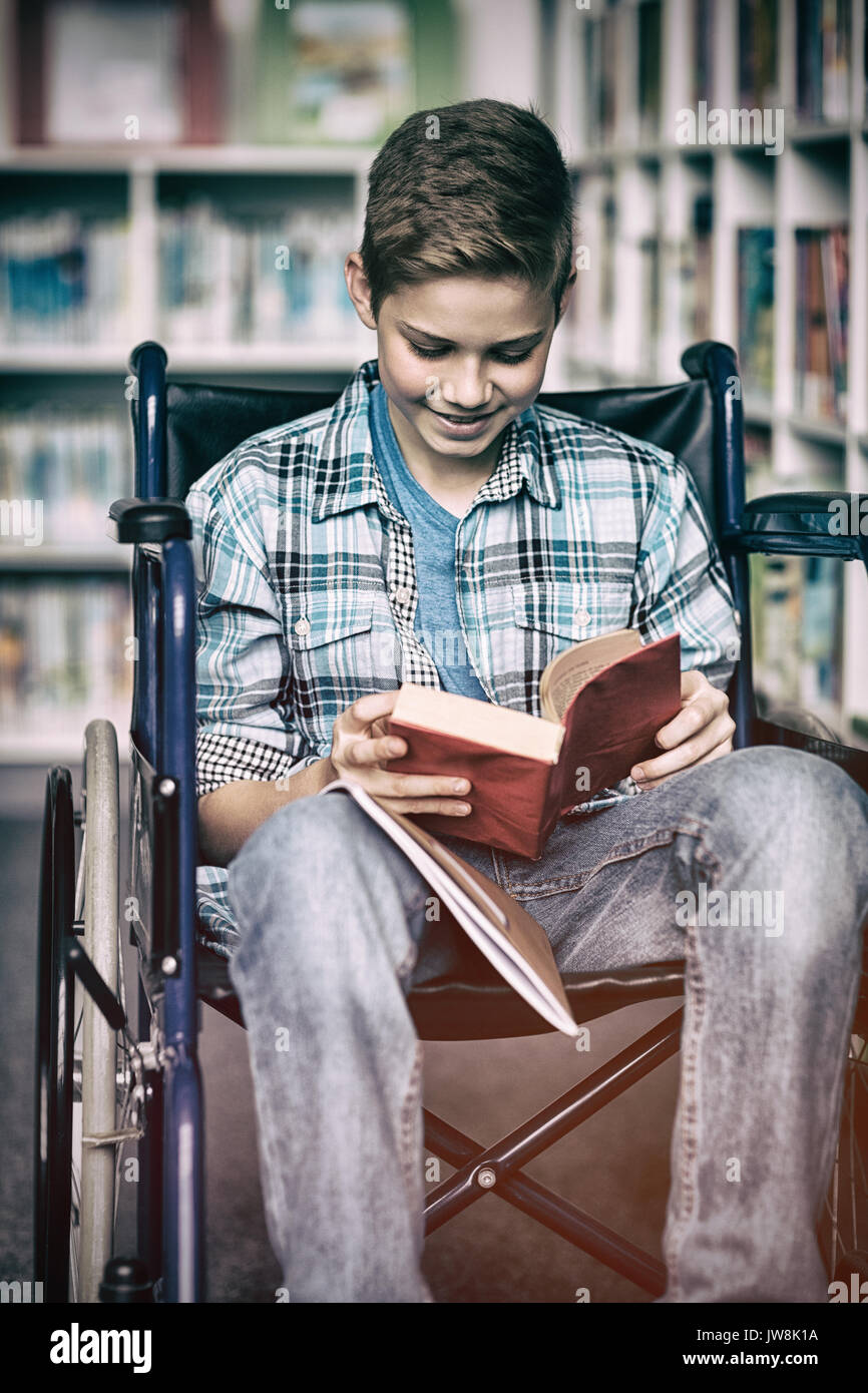 Disabled schoolboy reading book in library at school Stock Photo - Alamy