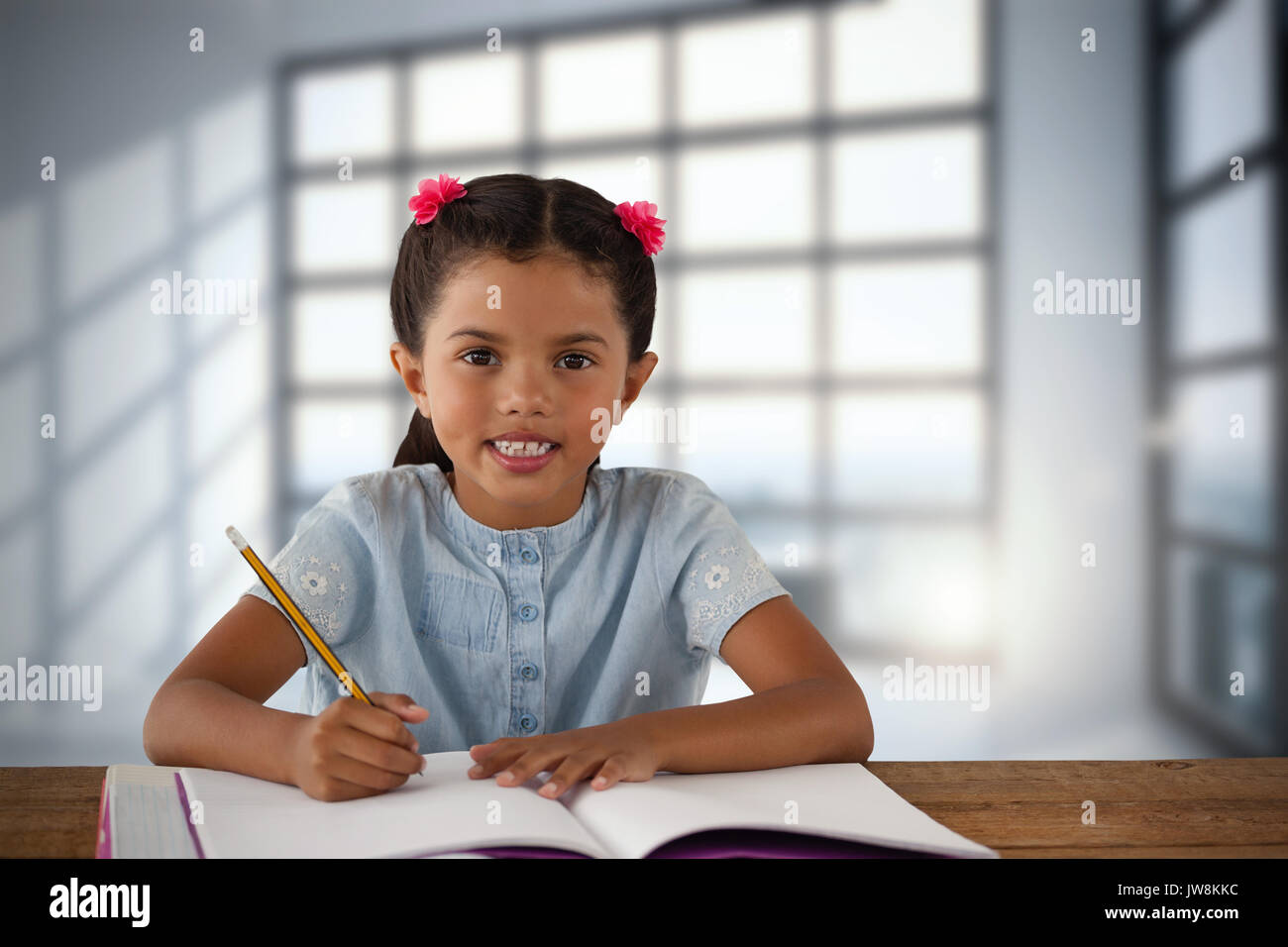 Smiling girl writing in book at desk against room with large windows ...