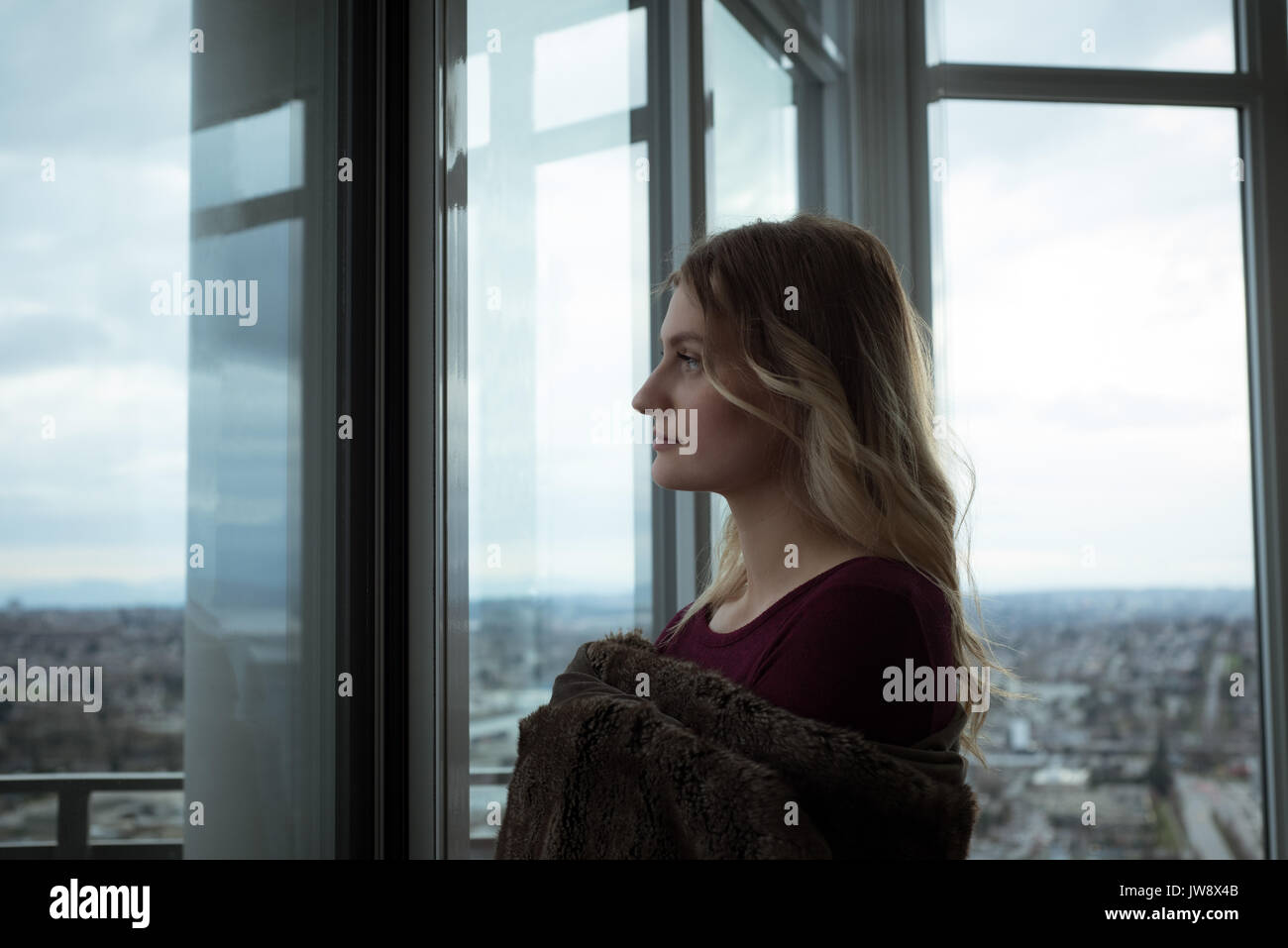Woman looking through the window in living room at home Stock Photo - Alamy
