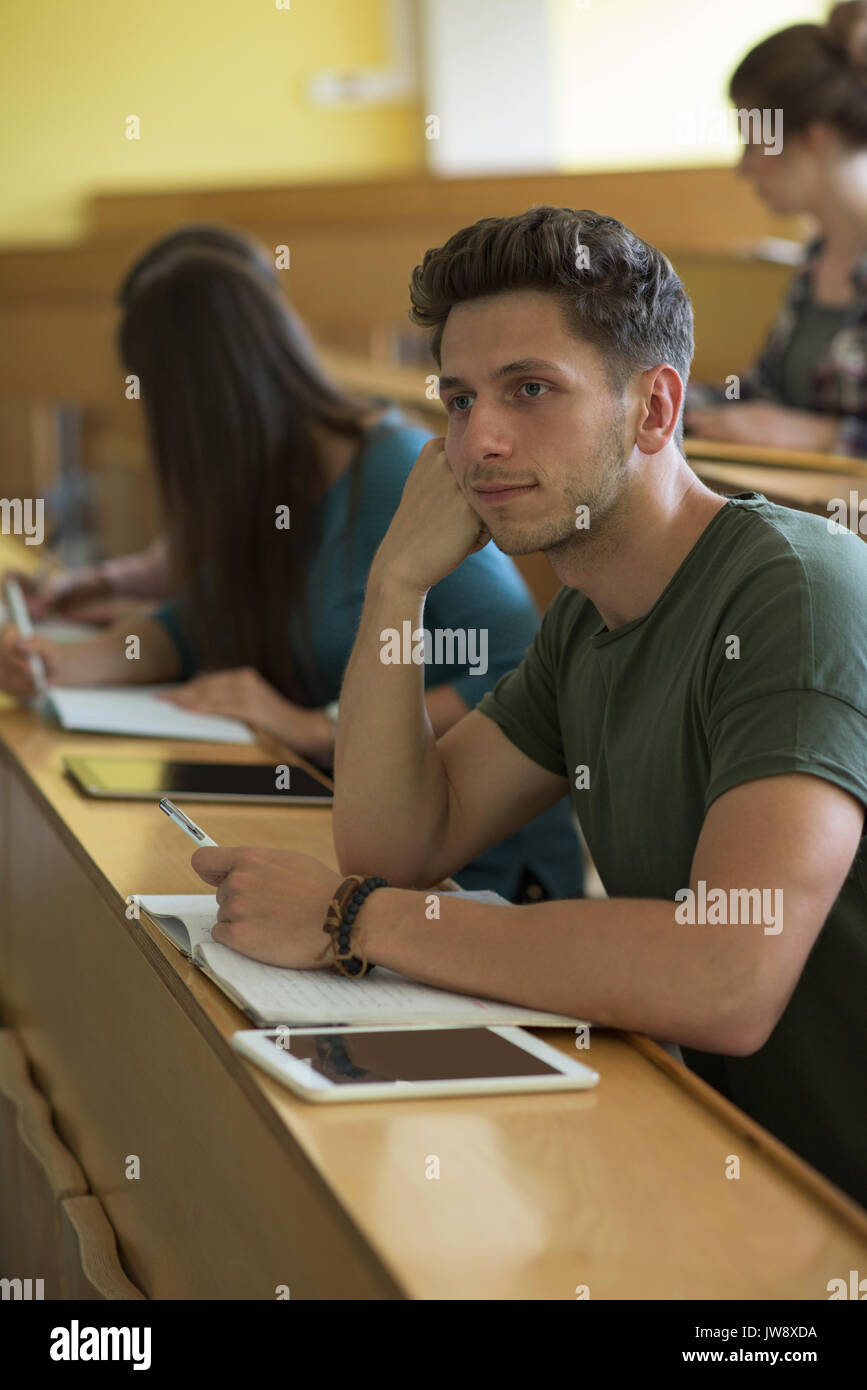 Thoughtful male student with classmates at desk in classroom Stock ...
