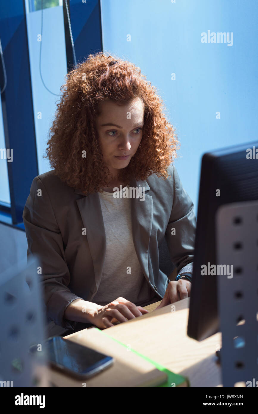 Female student using desktop computer while sitting at desk in ...