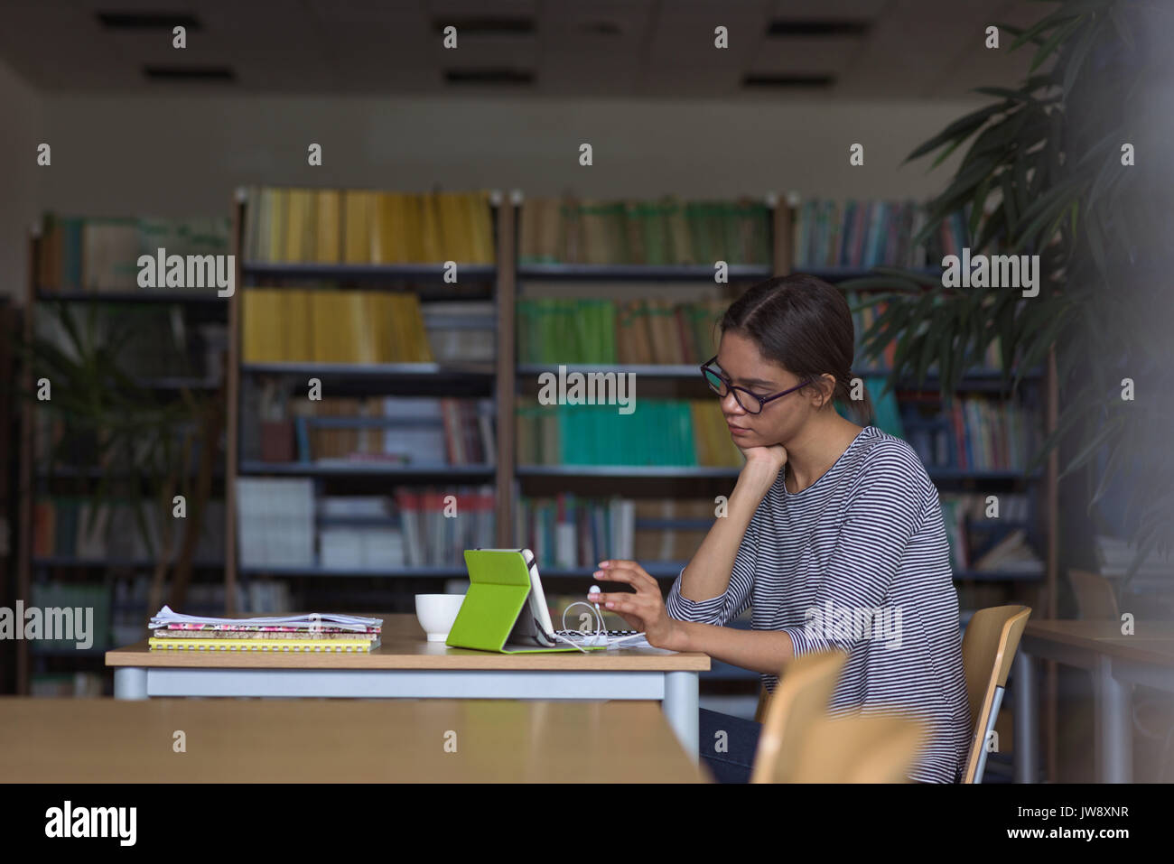 Female university student using digital tablet while sitting at desk in ...