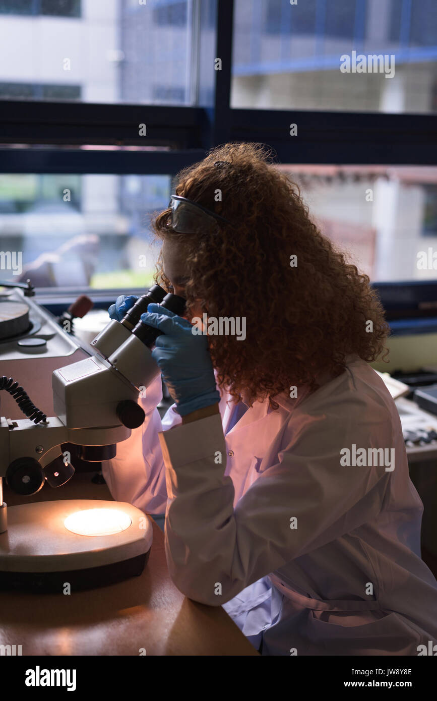 Side view of teenage girl using microscope while practicing experiment ...
