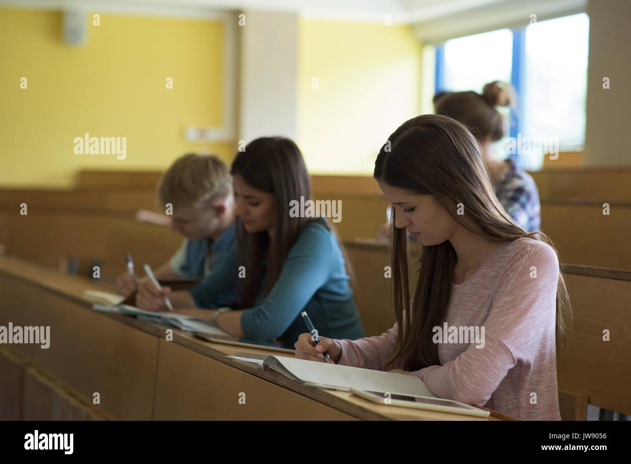 Young college students writing on book at desk while sitting classroom ...