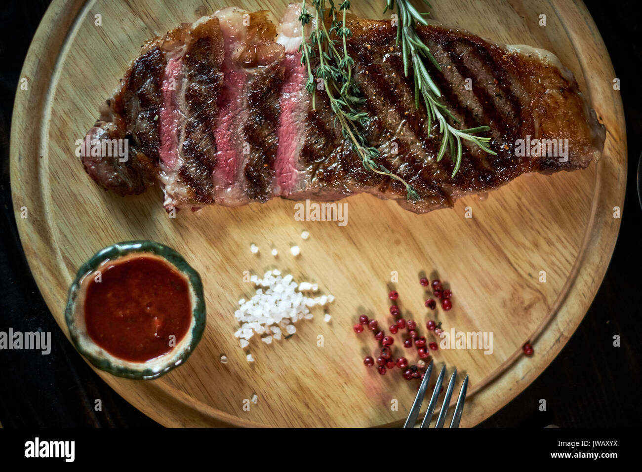 Sliced medium rare grilled steak on rustic cutting board with rosemary ...