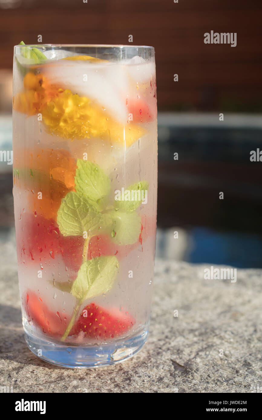 Glass of cold water infused with fruit, mint and edible flowers and ice ...