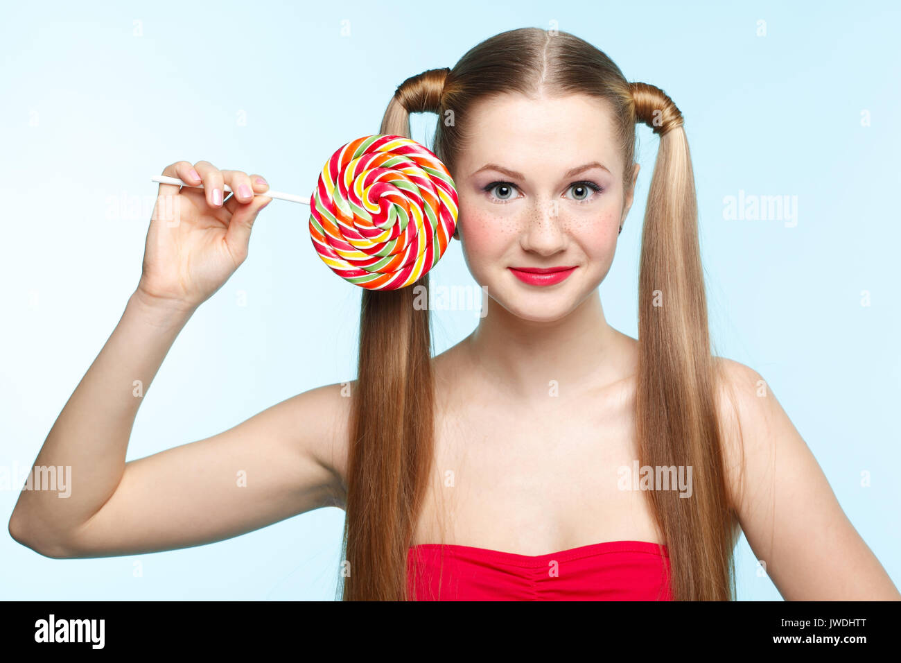 Beautiful playful young freckled girl with lollipop on blue background ...