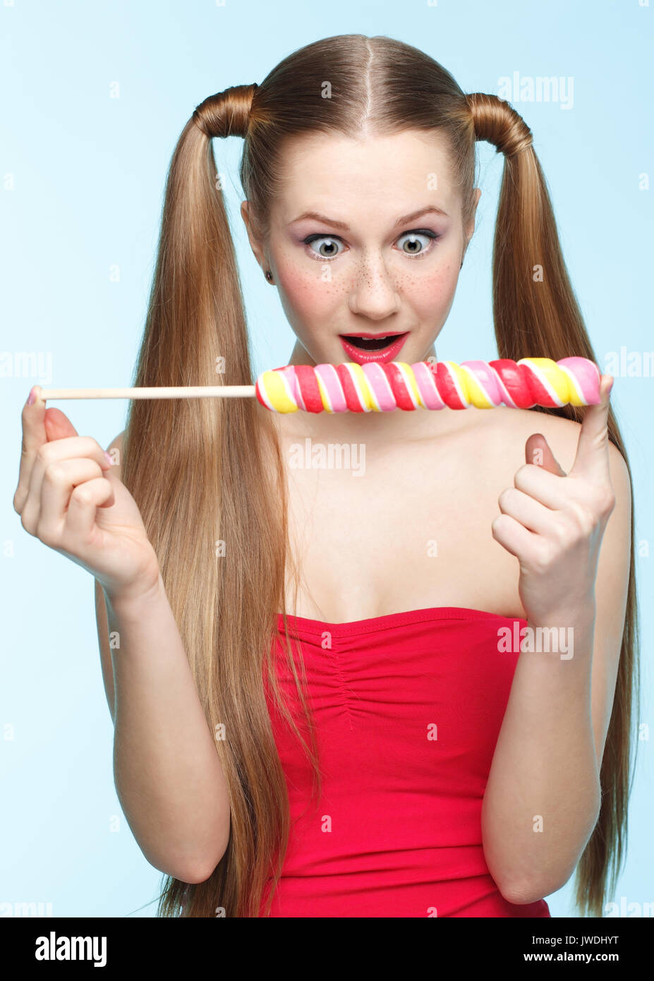 Beautiful playful young freckled girl with lollipop on blue background ...